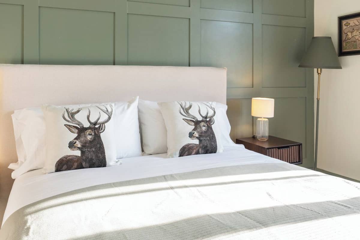 Cama com roupa de cama branca e duas almofadas com estampas de veados.