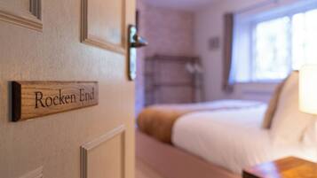 Quarto de hotel com cama, mesa de cabeceira, janela e porta com a placa 'Rocken End'.