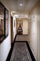 Um corredor de hotel com carpete listrado em preto e branco, quadros nas paredes e uma fileira de armários de um lado.