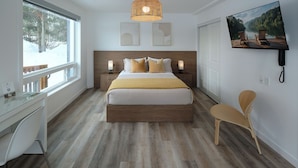 Um quarto moderno com uma cama grande, mesas de cabeceira, uma escrivaninha e uma televisão na parede.