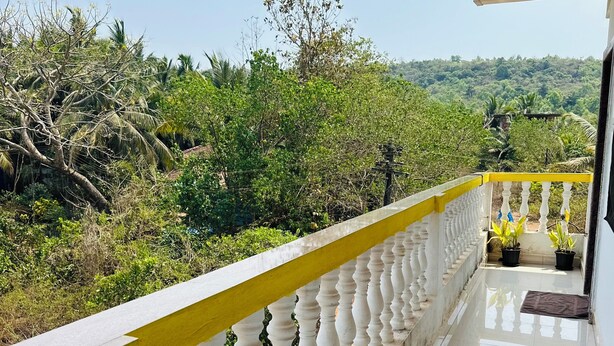 Varanda com guarda-corpo amarelo e branco com vista para uma paisagem verde exuberante.