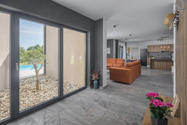Um interior moderno com área de estar, cozinha e grandes portas de vidro deslizantes que dão para uma área de piscina.