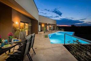 Uma área de piscina moderna ao ar livre, com espaço para refeições e espreguiçadeiras.