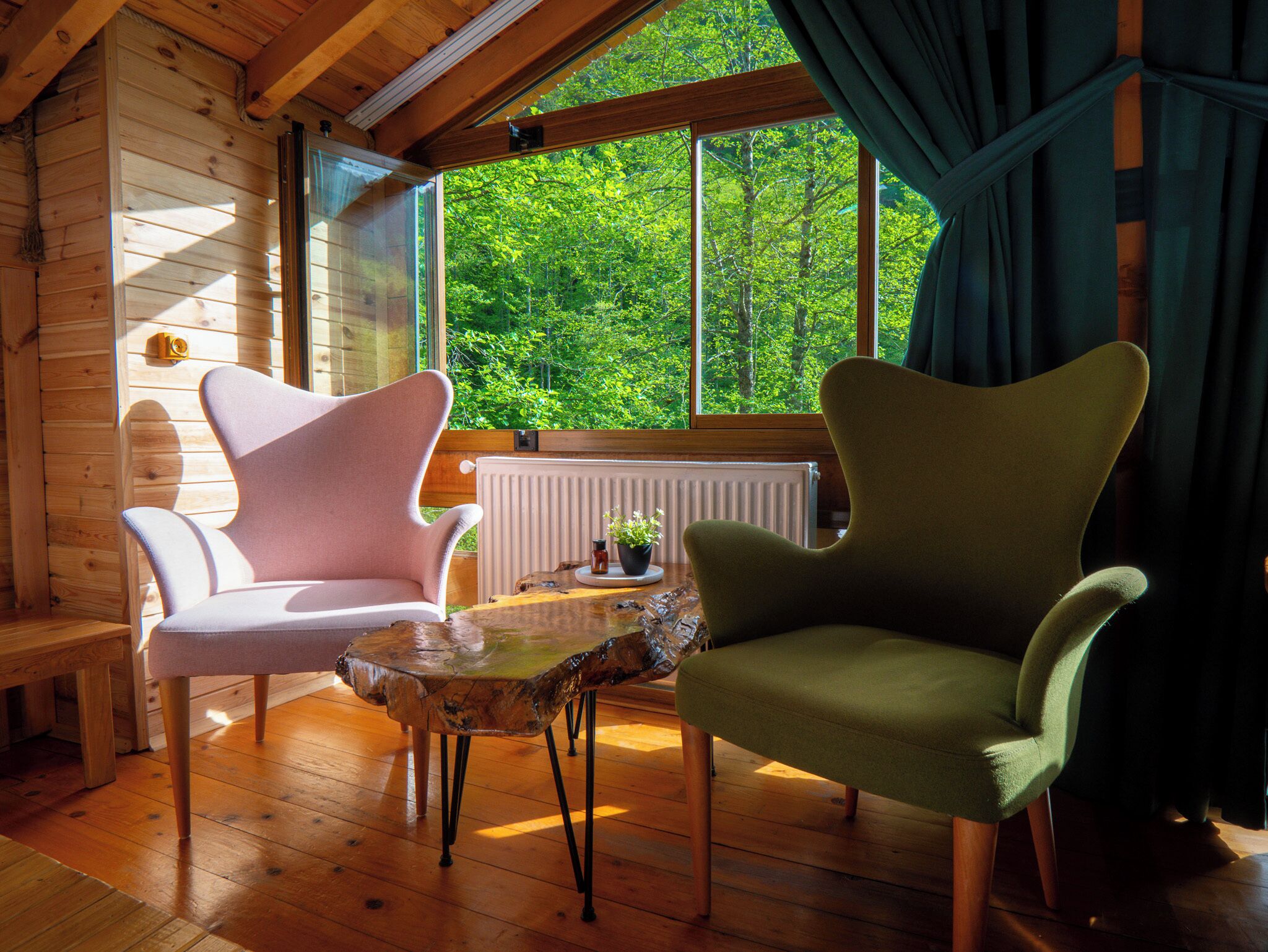 Interior acolhedor de uma cabana com duas cadeiras, uma mesa e uma janela com vista para uma floresta.