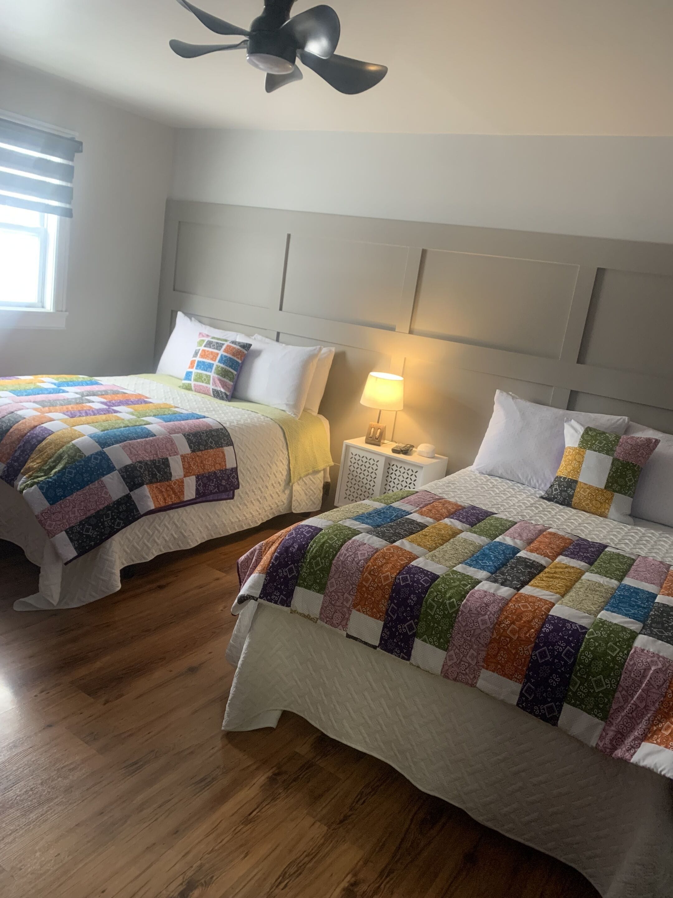 Quarto com duas camas, soalho de madeira, ventoinha no teto e uma mesa de cabeceira com abajur.