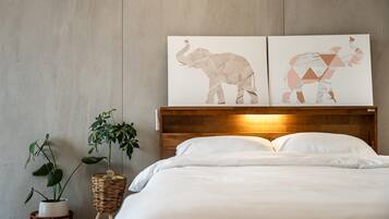 Quarto com cabeceira de madeira, duas obras de arte penduradas na parede com figuras abstratas, cama com lençóis brancos e duas plantas em vasos.