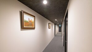 Um corredor com obras de arte emolduradas nas paredes, piso coberto de carpete e teto com iluminação embutida.