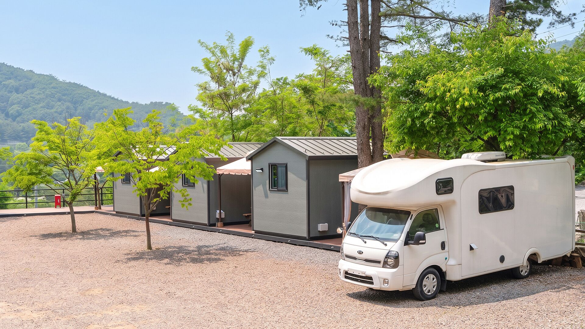 Uma RV branca estacionada em uma área de cascalho, com um pequeno prédio ao fundo.