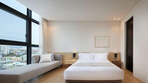 Quarto moderno com uma cama grande, um sofá e vista para a cidade.