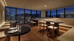 Área de refeições moderna com vista para a cidade, com mesa redonda, mesa retangular e diferentes disposições de assentos.