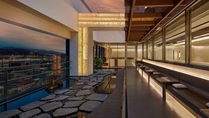 Um corredor de hotel moderno com caminho de pedra, áreas de estar e vista para a paisagem urbana.