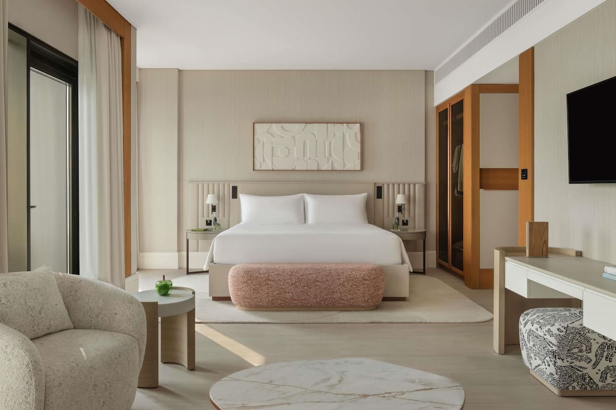Quarto de hotel moderno com uma cama grande, mesas de cabeceira, escrivaninha, cadeira e televisão.