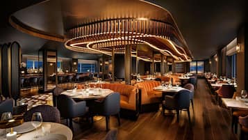 Restaurante moderno com área de estar central e teto iluminado em curva. Mesas montadas com taças de vinho e pratos, e um ambiente acolhedor e convidativo.