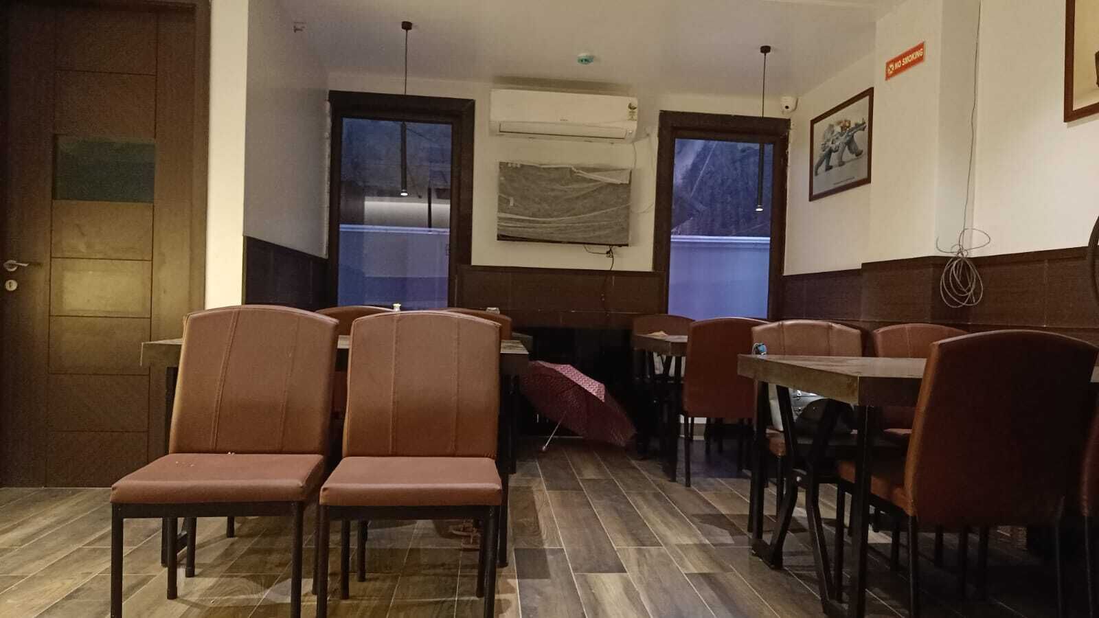 Um restaurante com chão de madeira, cadeiras de couro marrom e mesas. Há unidades de ar condicionado nas paredes e um sinal de 'No Smoking'.