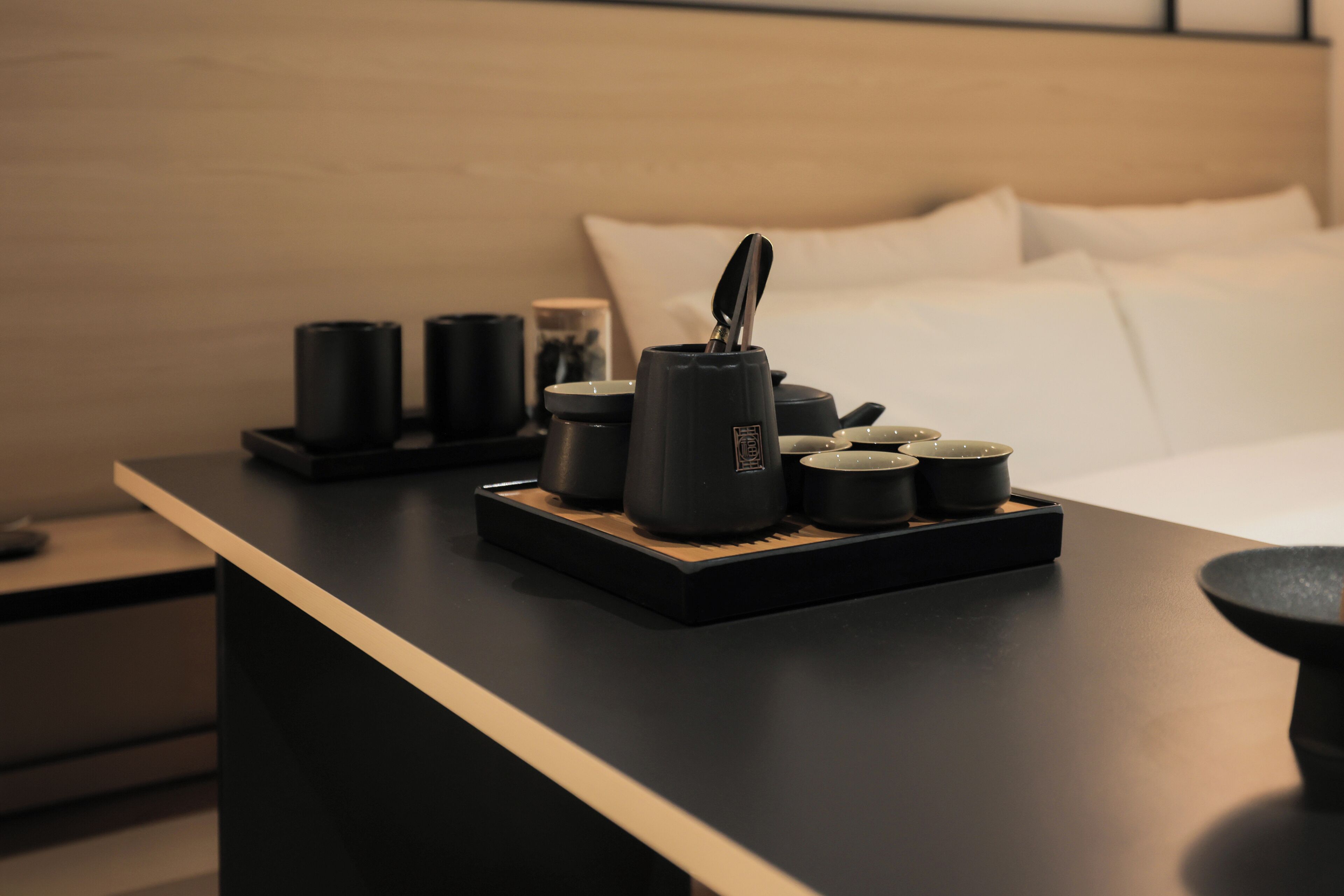 Uma bandeja organizada com xícaras pretas e uma chaleira sobre uma bancada escura em quarto de hotel.