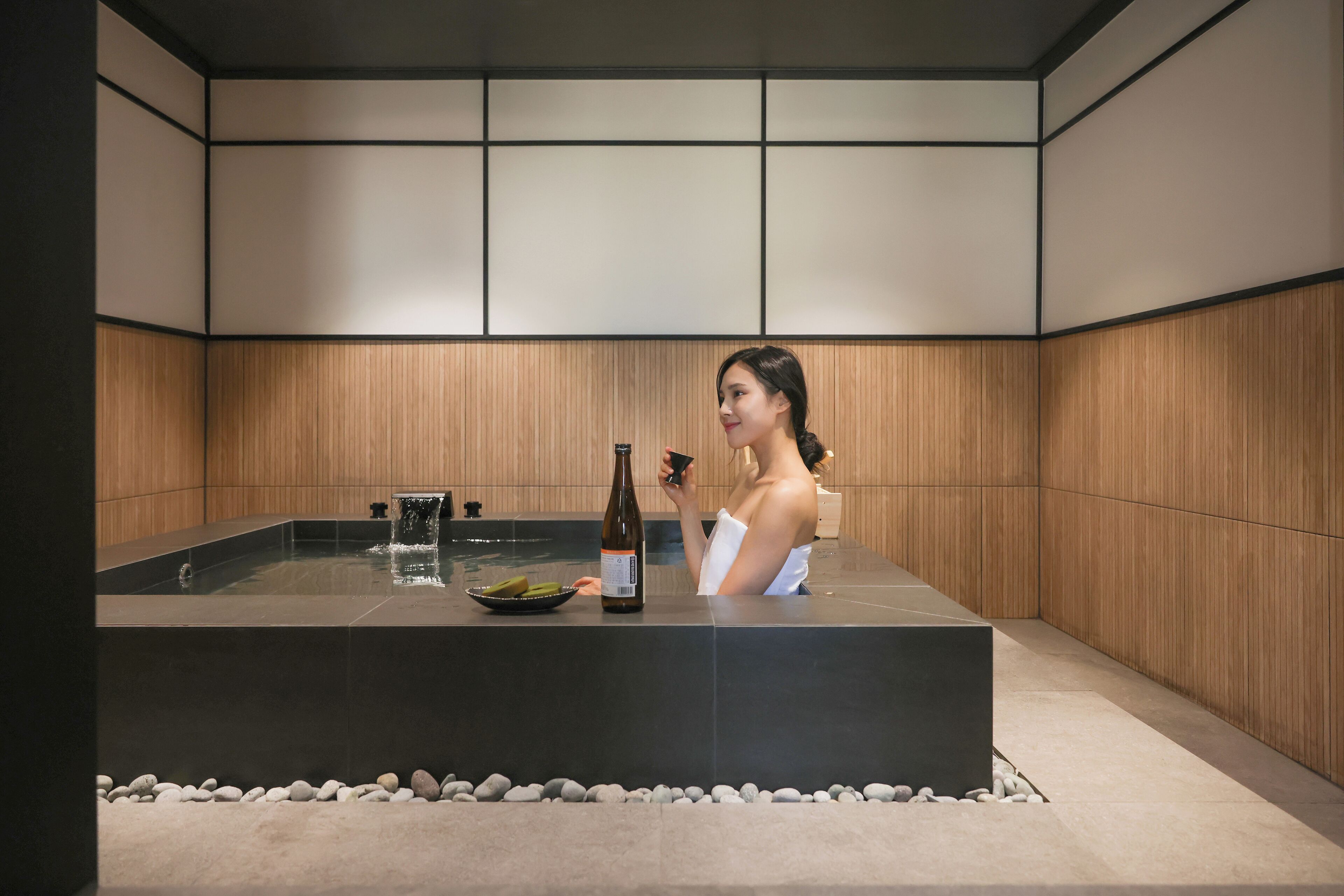 Uma área de spa com uma banheira grande, uma garrafa de vinho e uma tábua de frutas.