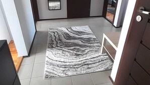 Um quarto espaçoso com um tapete grande de padrão marmorizado, uma porta de madeira escura e um espelho na parede.