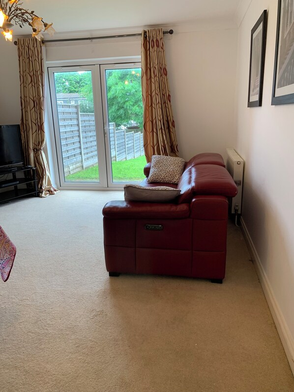 Uma sala de estar com um sofá vermelho, uma televisão e uma porta de vidro deslizante que dá para um jardim.