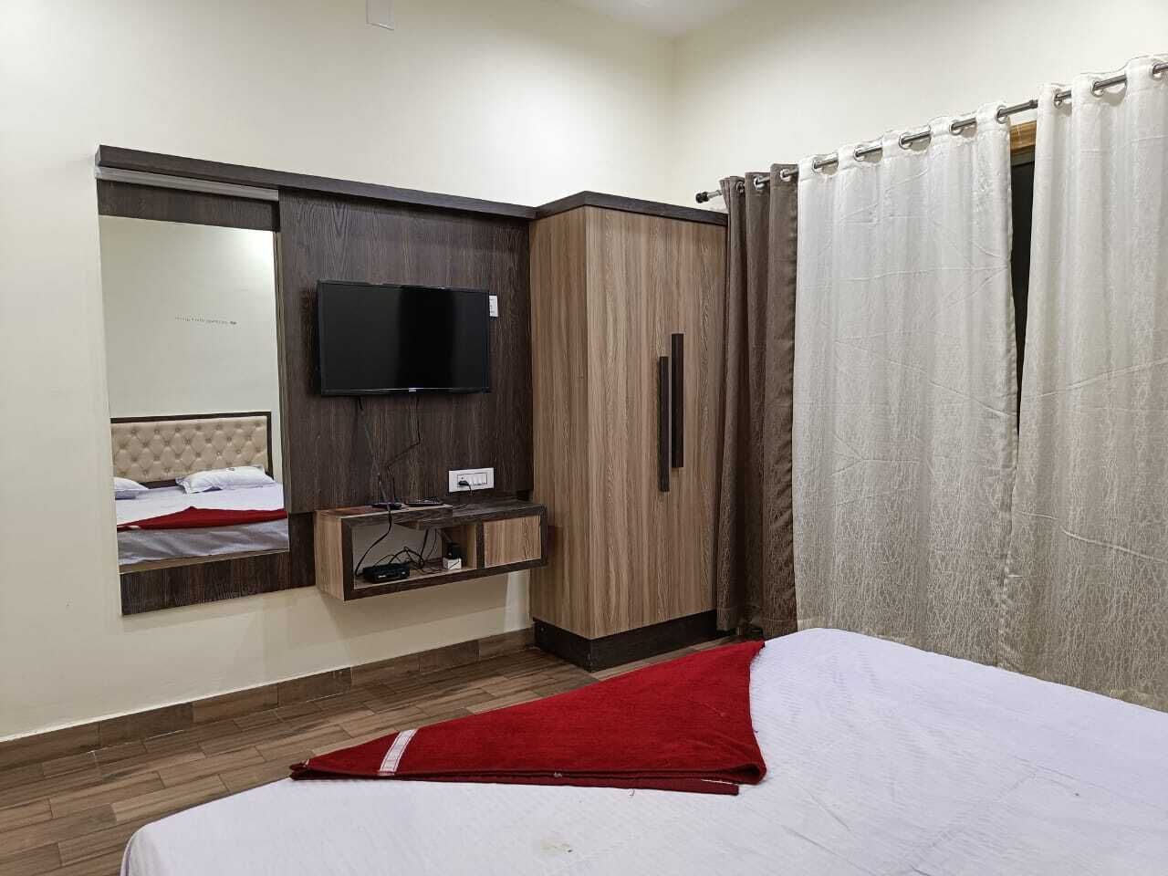 Quarto de hotel com cama, televisão na parede, guarda-roupa e cortina.