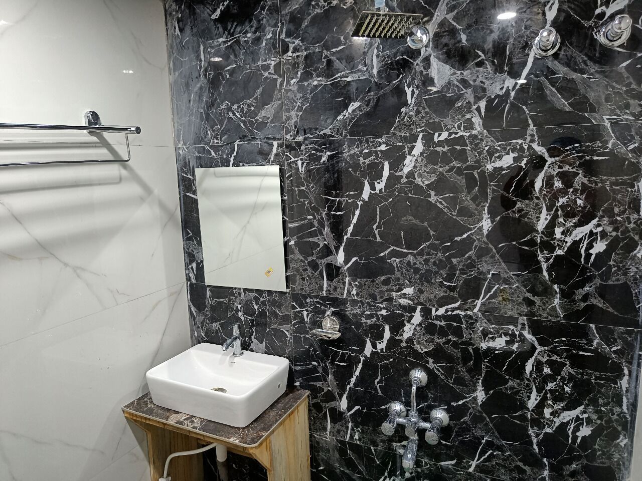Casa de banho com uma pia branca, um espelho e uma parede de mármore preto.