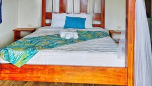Uma cama de madeira com dossel, roupa de cama branca, um travesseiro azul e um edredom com motivos tropicais.