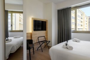 Quarto de hotel com duas camas, televisão na parede, uma cadeira e janela com cortinas.