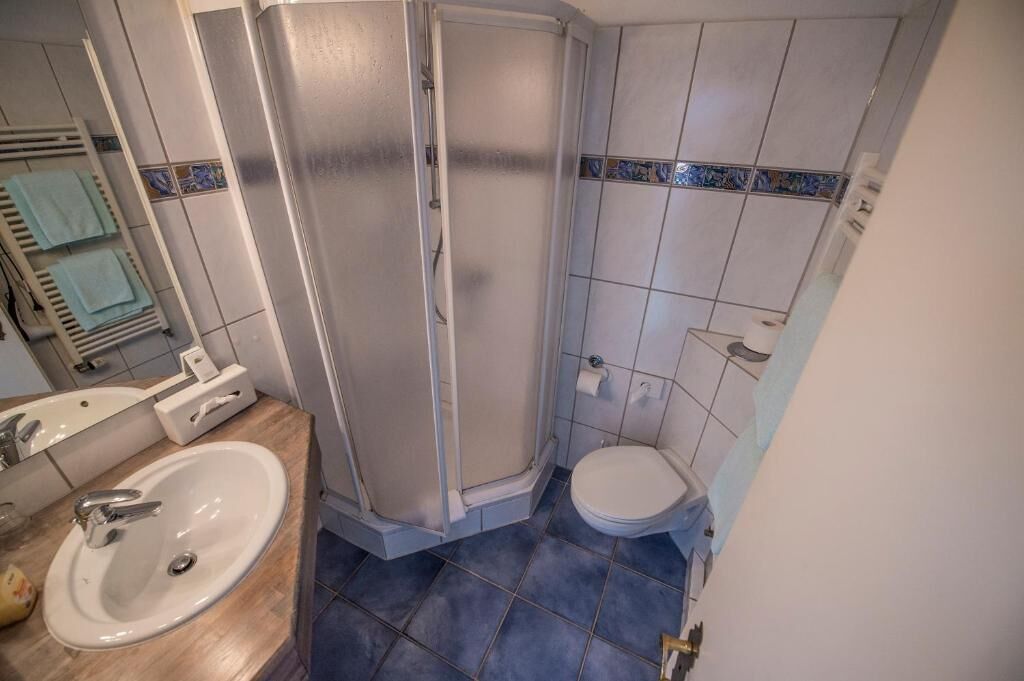 Casa de banho com chuveiro, sanita, lavatório e porta-toalhas.