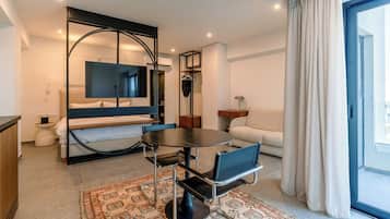 Quarto de hotel moderno com sofá, mesa de jantar com cadeiras, televisão e uma grande janela com cortinas.