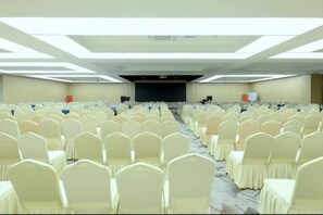 Uma sala de conferências com fileiras de cadeiras, um palco e uma tela de projeção.