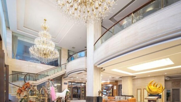 Um hall espaçoso com um imponente candelabro, uma escadaria e uma área de recepção.