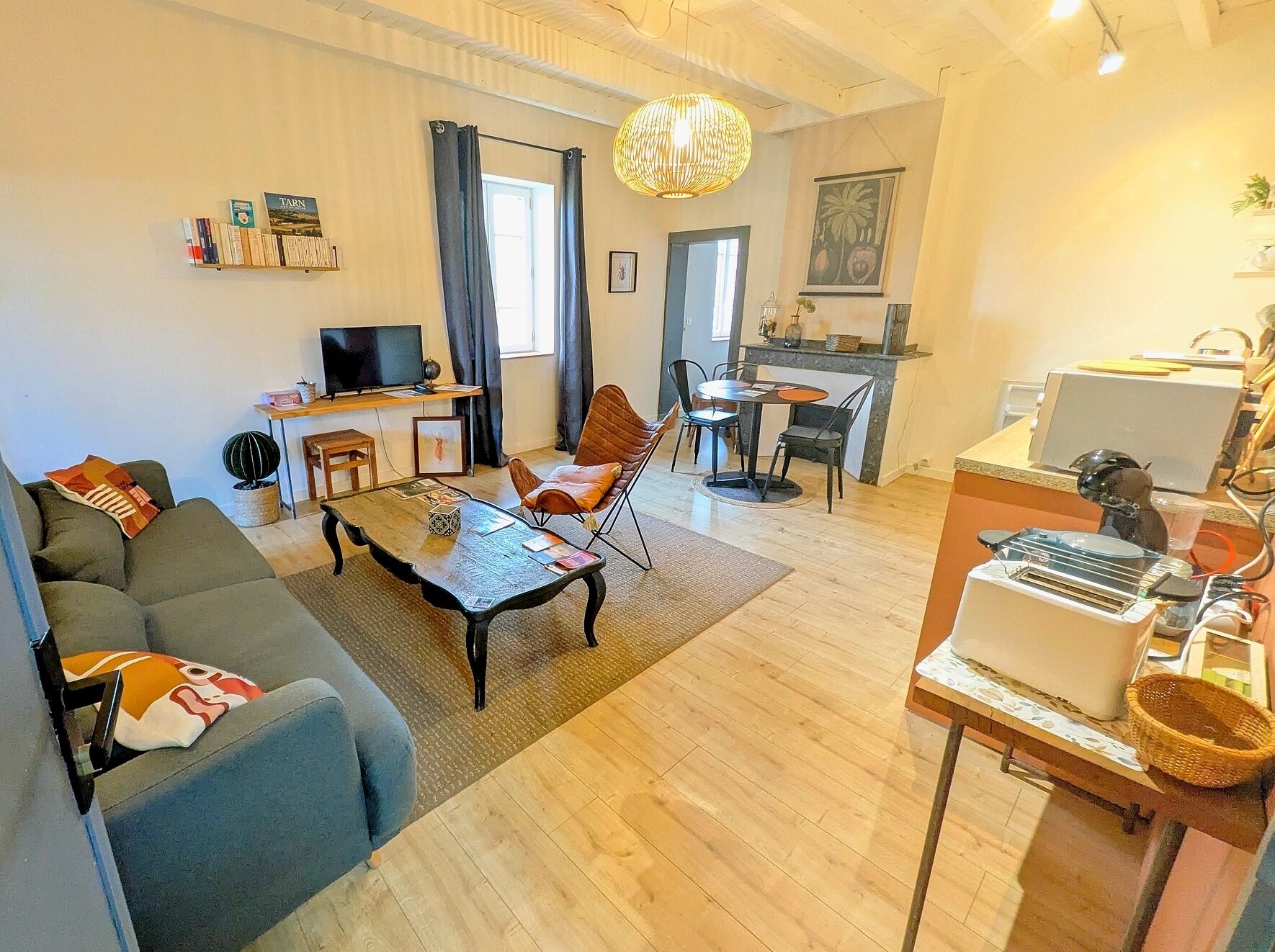 Uma sala de estar com sofá, mesa de centro e poltronas, uma televisão, um espaço de jantar com mesa e cadeiras, e uma cozinha com geladeira e micro-ondas.