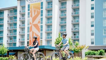 Duas pessoas andando de bicicleta em frente a um hotel com uma grande placa indicando