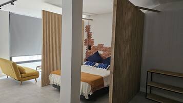 Quarto moderno com cama, poltrona amarela, divisória de madeira e parede de tijolos como destaque.