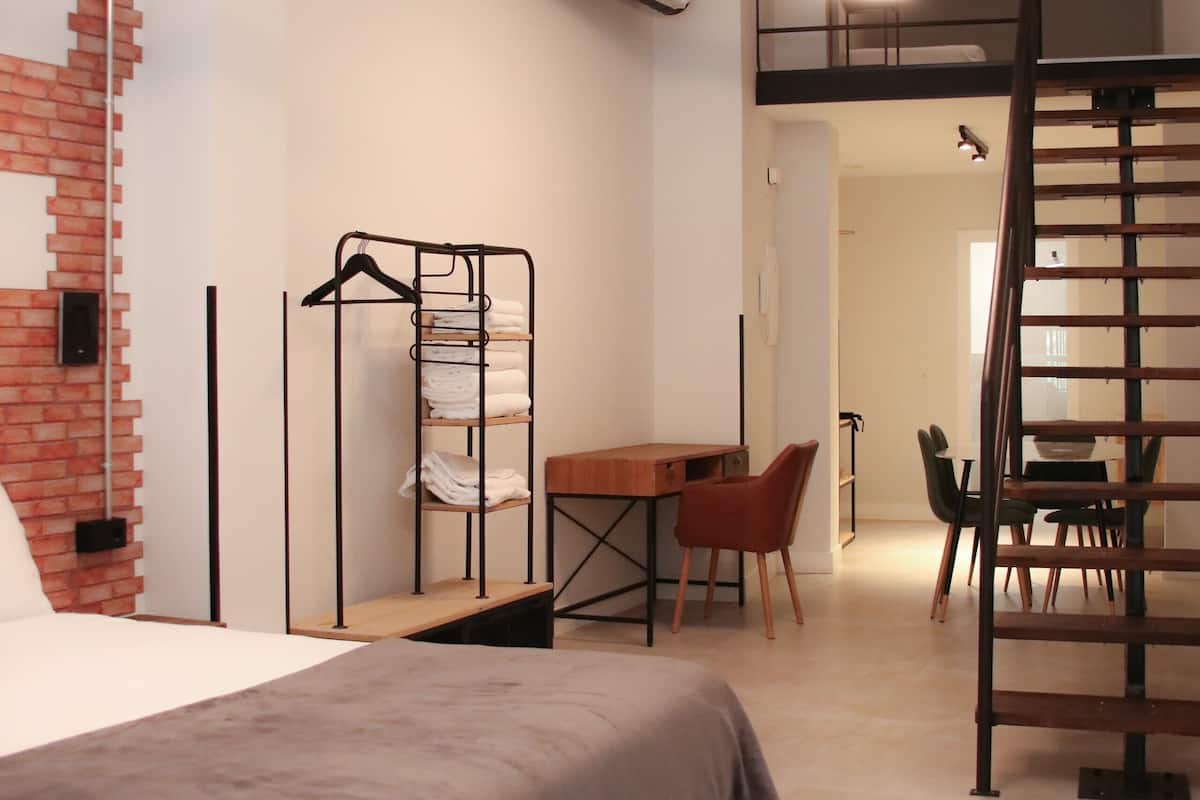 Quarto moderno com cama, escrivaninha e cadeira. Apresenta luminária pendente e parede de tijolos.