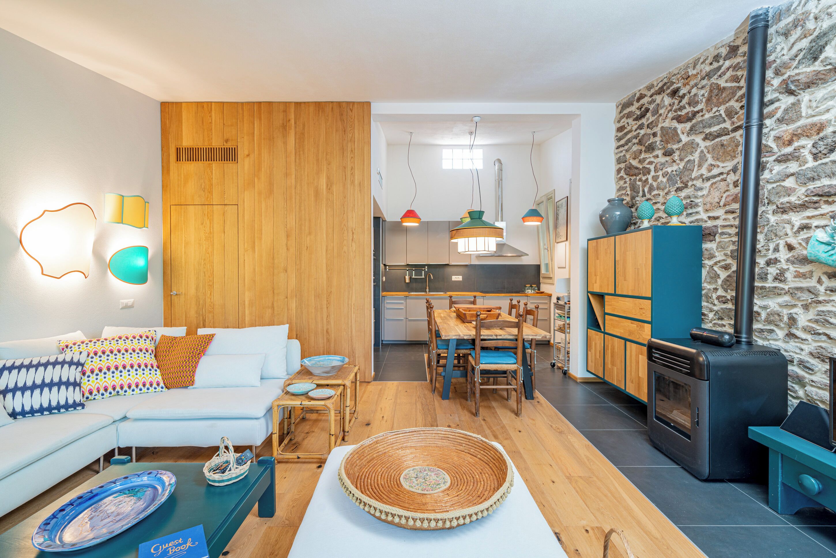 Uma sala de estar moderna com sofá, mesa de centro e área de refeições com cadeiras e mesa. Uma cozinha com fogão e armários é visível ao fundo.
