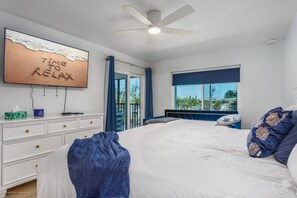 Um quarto com cama, ventilador de teto, janela com vista, cômoda e uma televisão na parede exibindo 'TIME TO RELAX'.