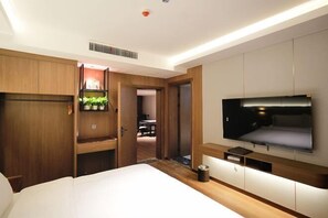 Quarto de hotel moderno com uma cama grande, televisão de tela plana na parede, mobiliário de madeira e uma pequena planta em uma prateleira.