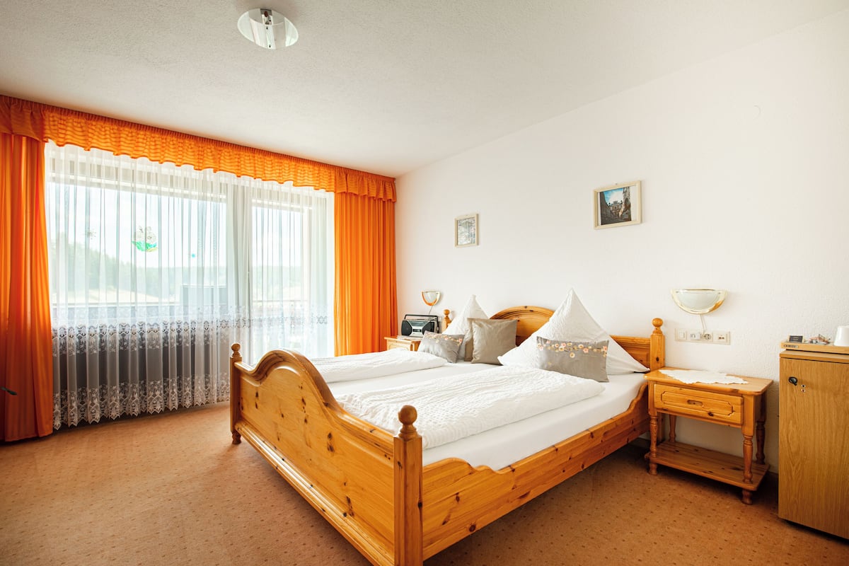Quarto com cama de madeira, mesa de cabeceira, cômoda e janela com cortinas.