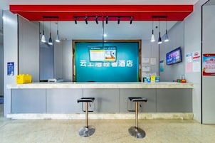 Recepção de hotel com balcão, dois bancos altos, teto vermelho e uma tela digital exibindo informações.
