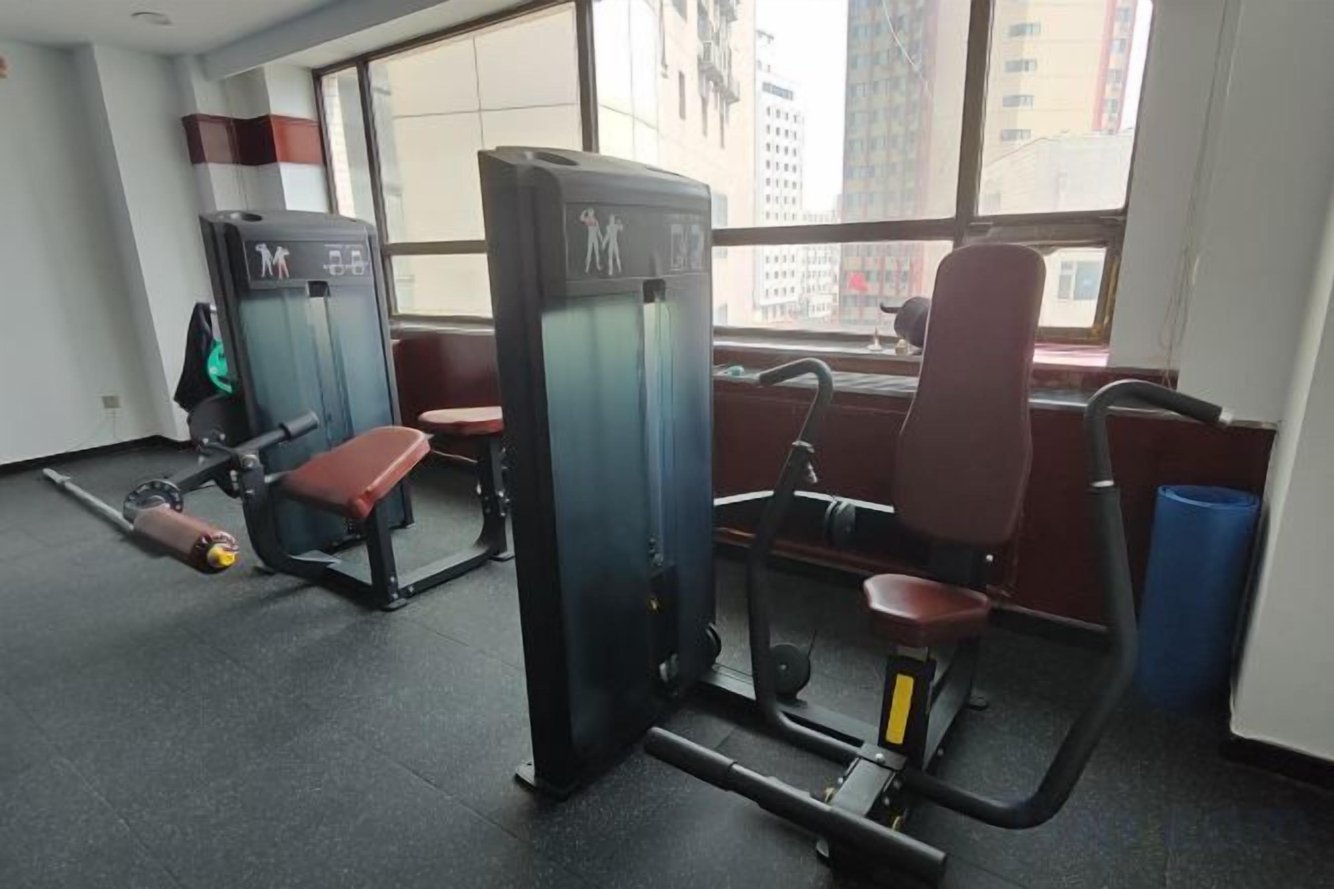 Academia com equipamentos de ginástica, um banco e uma janela com vista para a cidade.