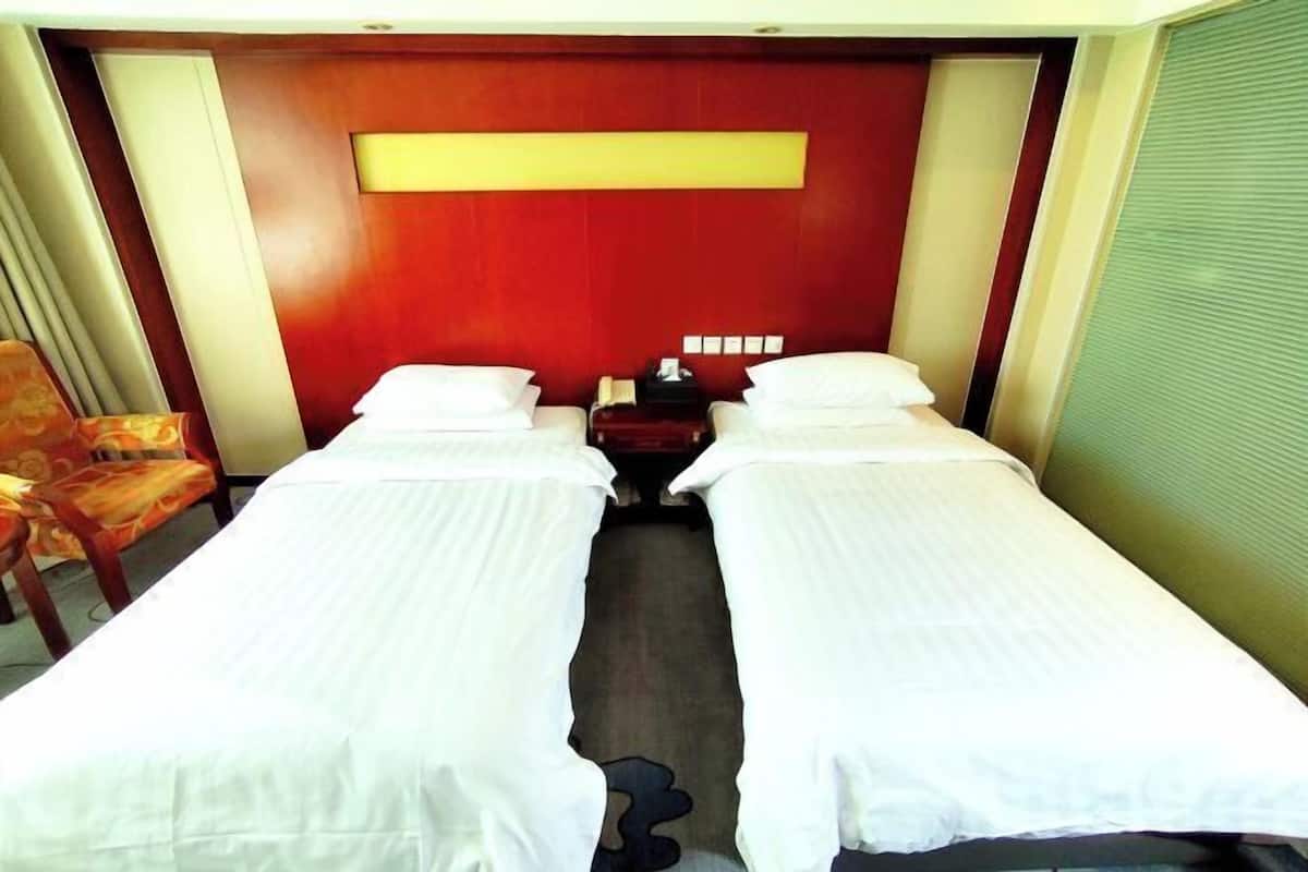 Quarto de hotel com duas camas de solteiro, cabeceira de madeira, mesa de cabeceira e uma cadeira.