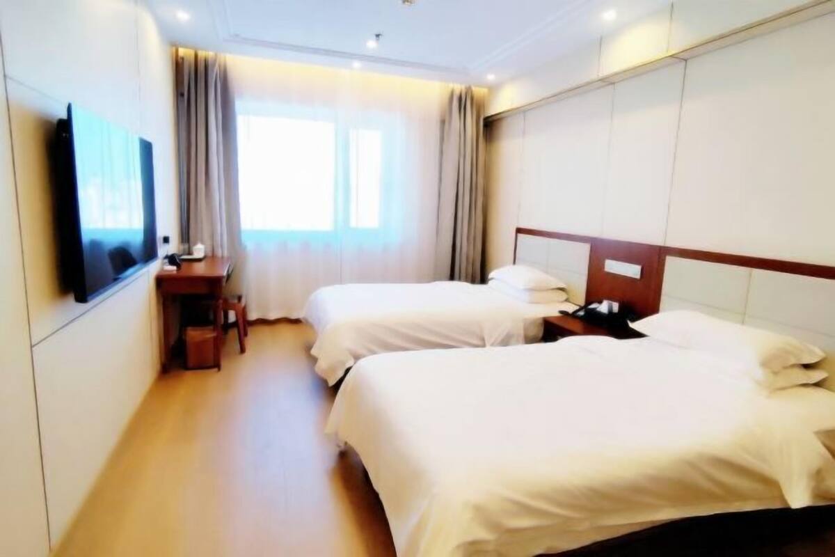 Quarto de hotel com duas camas, televisão, escrivaninha e janela com cortinas.