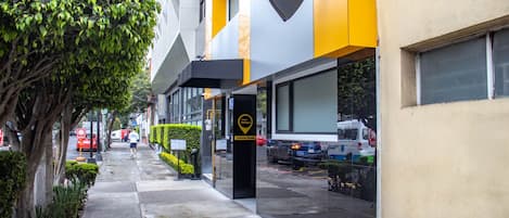 Um hotel chamado 'HOTELES ESCALA' com fachada moderna, entrada visível e área de estacionamento com veículos.