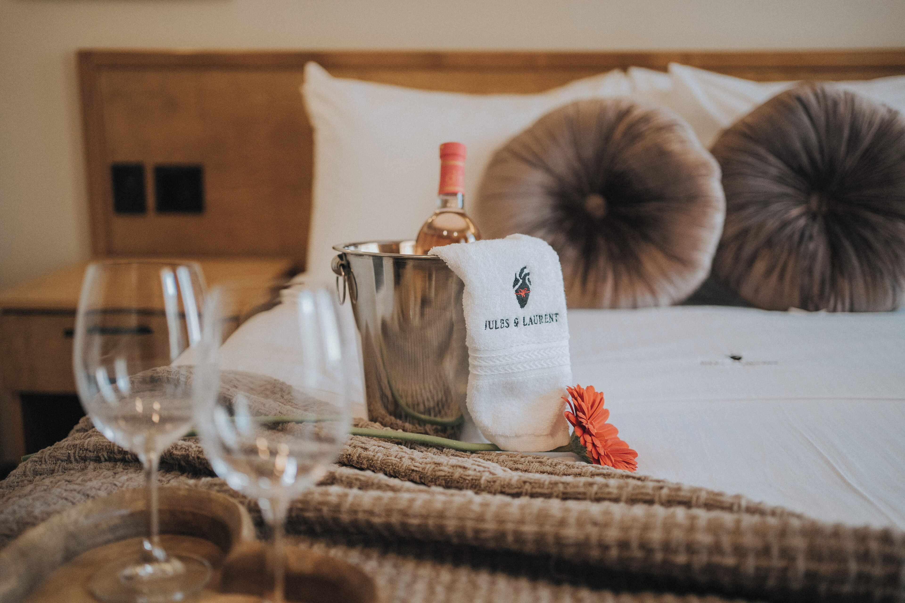 Uma cama com uma garrafa de vinho, um copo e uma toalha com a inscrição 'Jules & Laurent'.