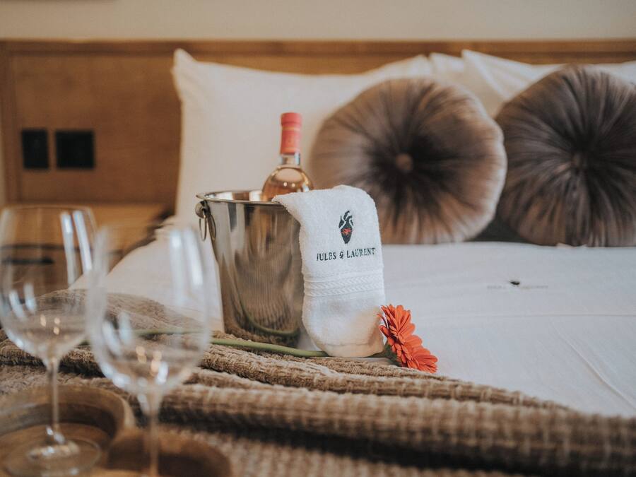 Uma cama com uma garrafa de vinho, um copo e uma toalha com a inscrição 'Jules & Laurent'.