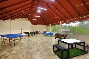 Uma área de lazer ampla e coberta, com mesa de tênis de mesa, mesa de futebol e mesa de bilhar.