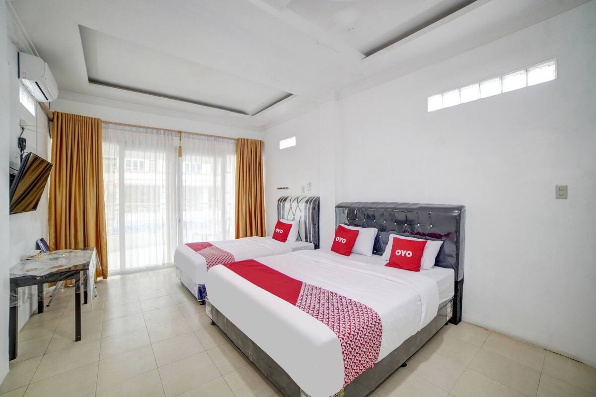 Quarto de hotel com uma cama grande, duas mesas de cabeceira, uma escrivaninha e uma janela com cortinas.