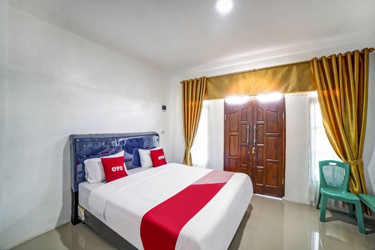 Quarto de hotel com uma cama, uma porta de madeira e uma cadeira verde.