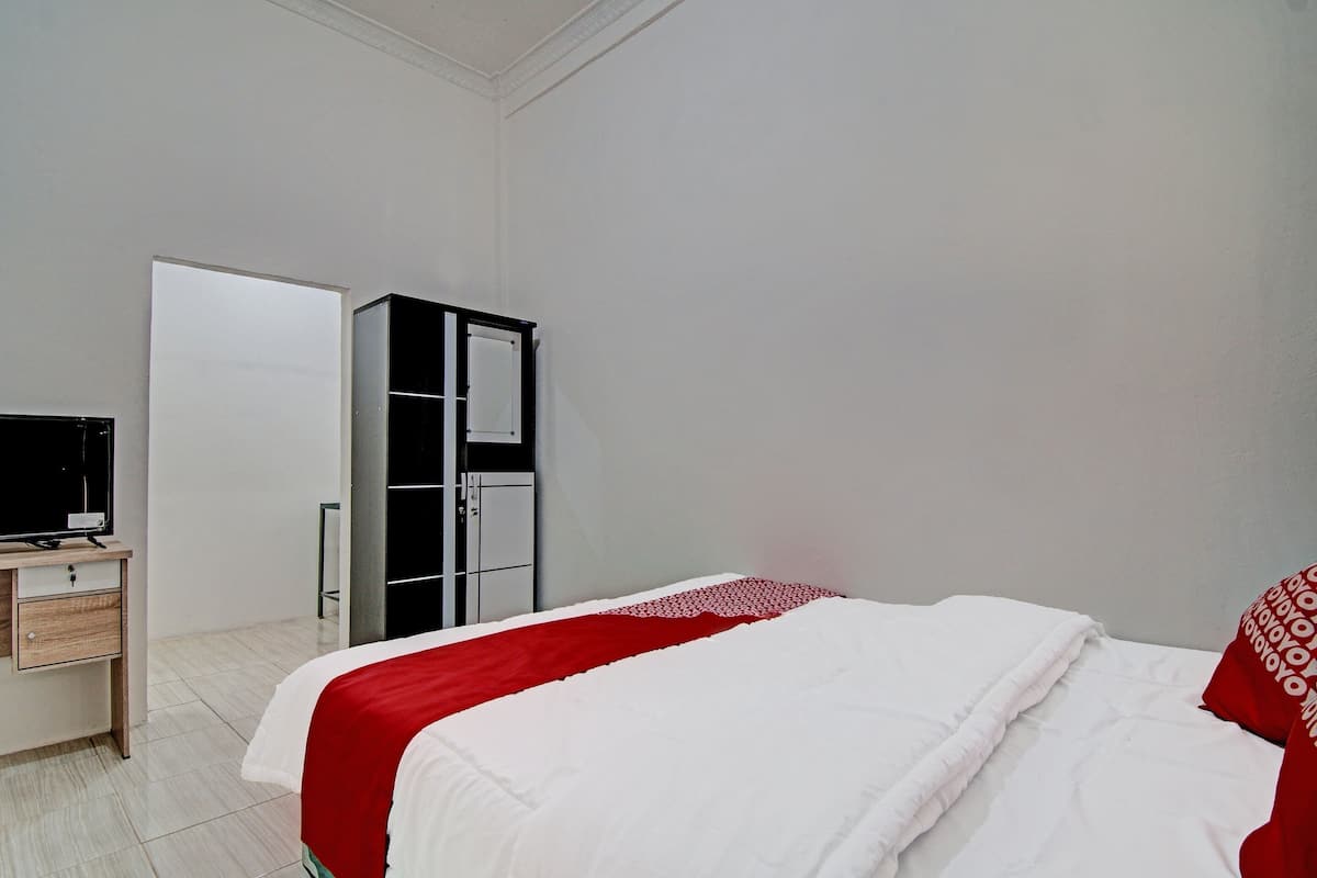 Quarto com cama, guarda-roupa, escrivaninha com computador e porta para outro espaço.