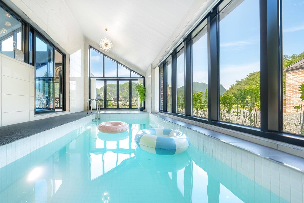 Piscina interna com paredes de vidro transparente, chão ladrilhado e dois flutuadores infláveis.